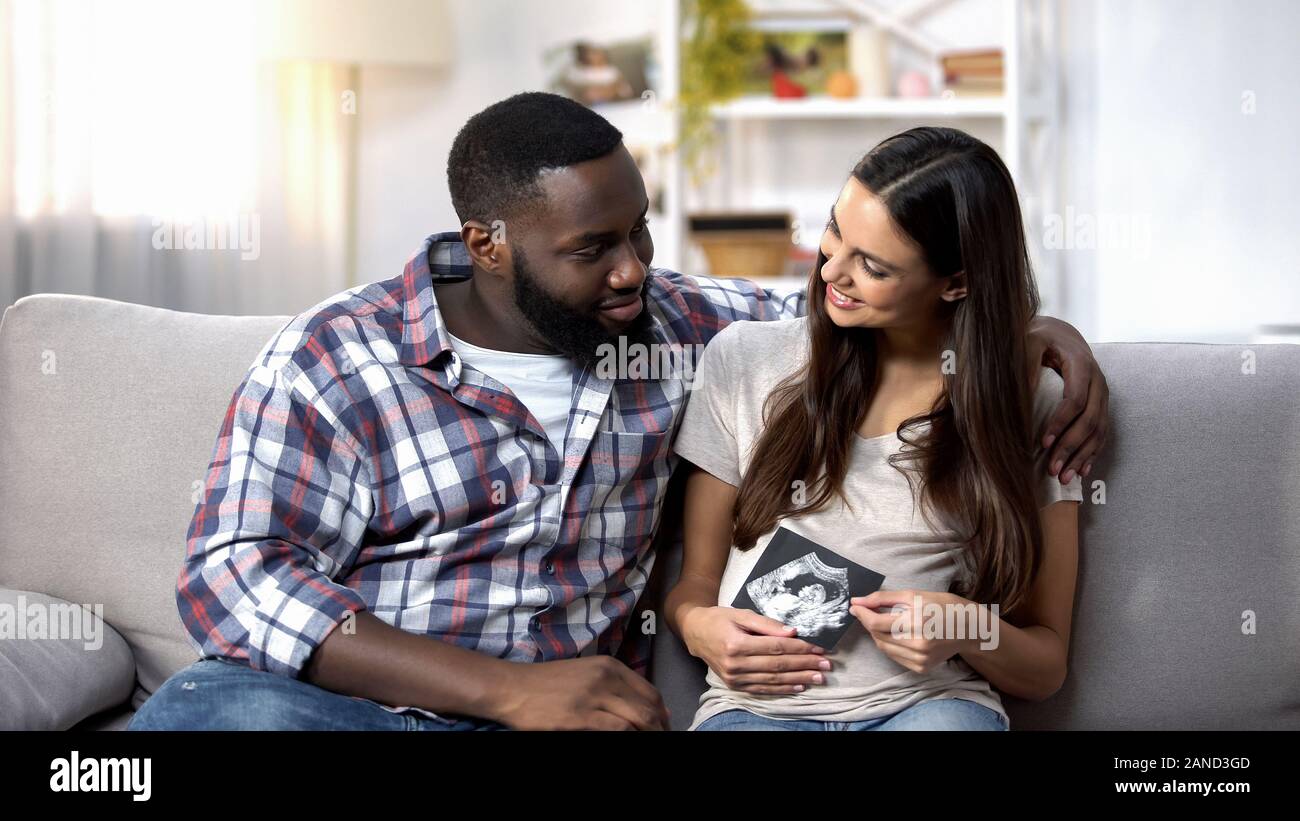 Joyful multiracial couple looking on baby x-ray, happy family ...