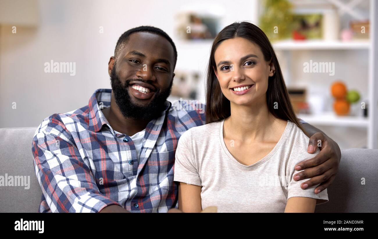 Smiling multiracial couple hugging and looking to camera, social ...