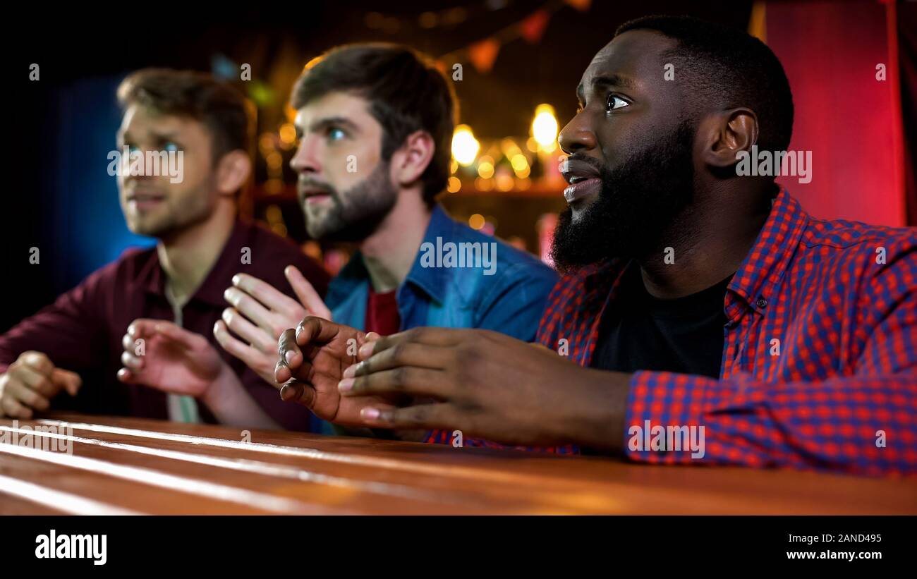 Three multiethnic friends watching song contest on tv in bar, ready for ...