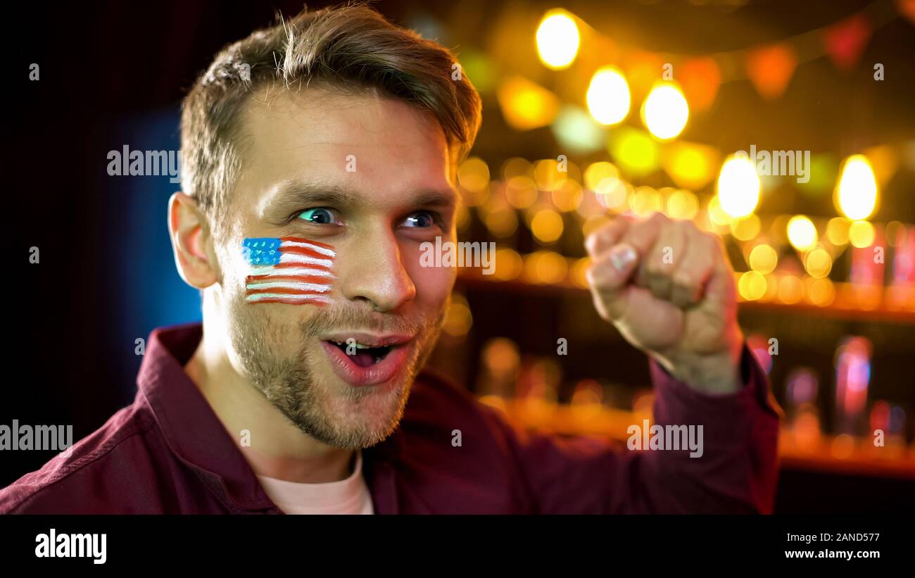 Emotional american football fan with flag on cheek making yes gesture ...