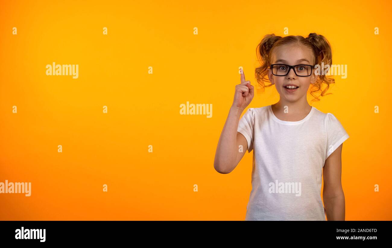Funny nerd schoolgirl raising finger up isolated on orange background ...
