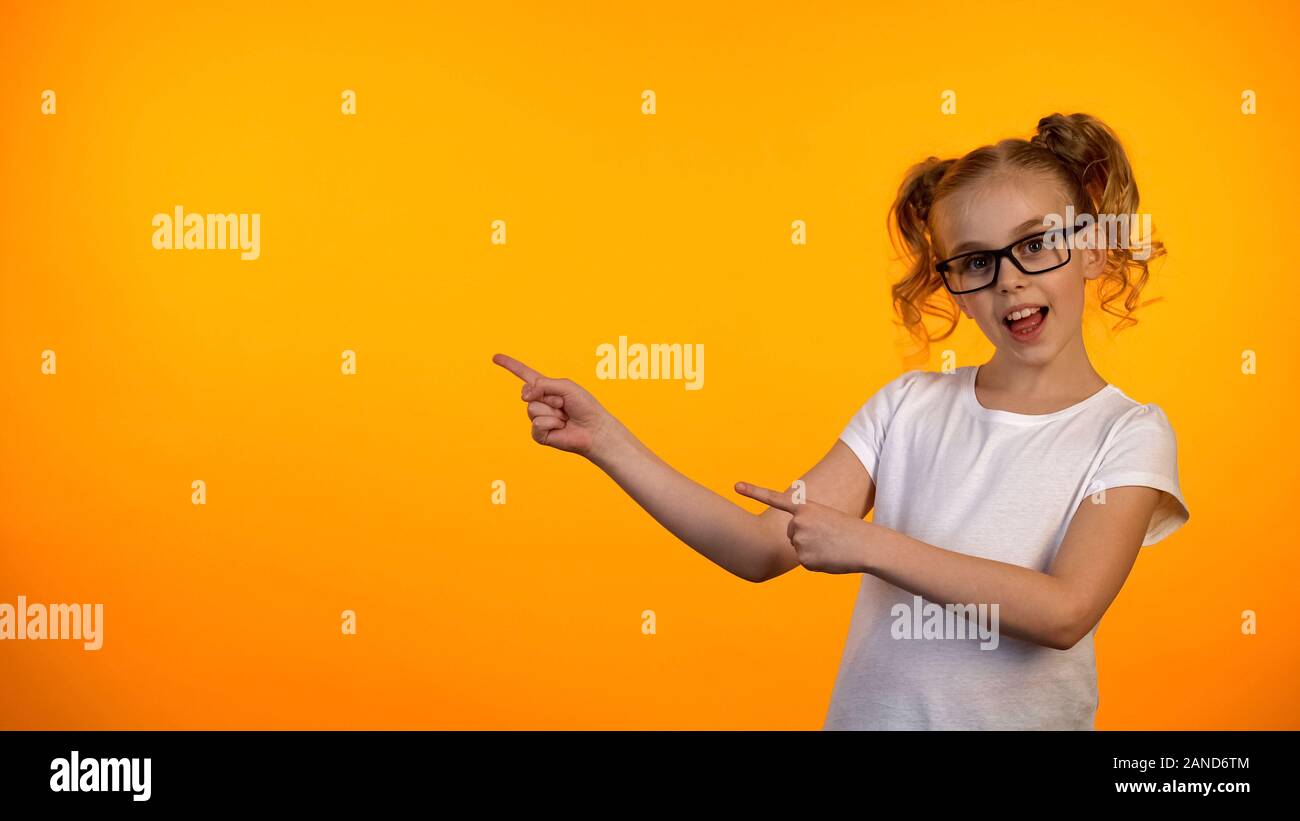 Pretty nerd girl in glasses pointing at orange background, education ...
