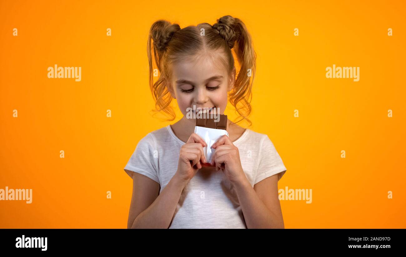 Adorable little girl biting delicious chocolate enjoying sweet taste ...