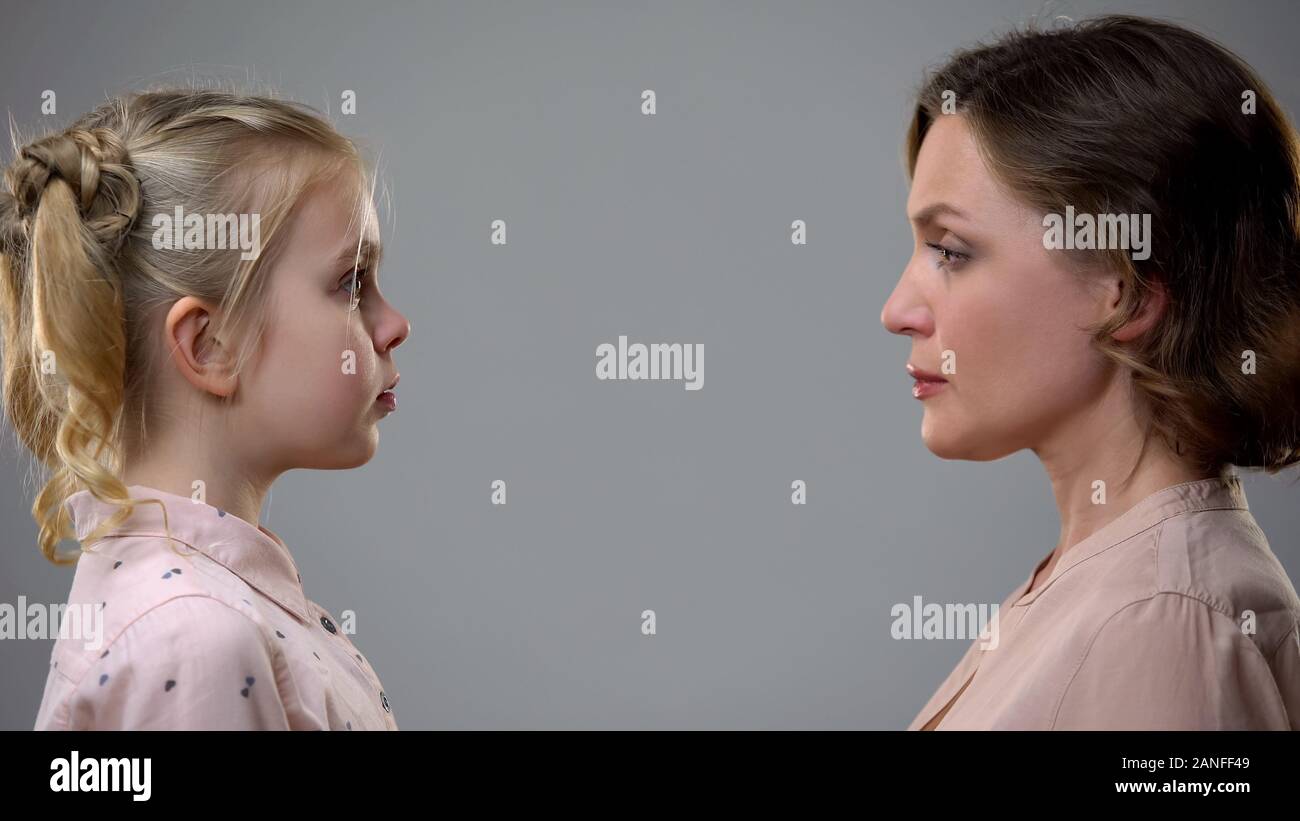 Strict mother looking scared daughter on grey background, discipline ...