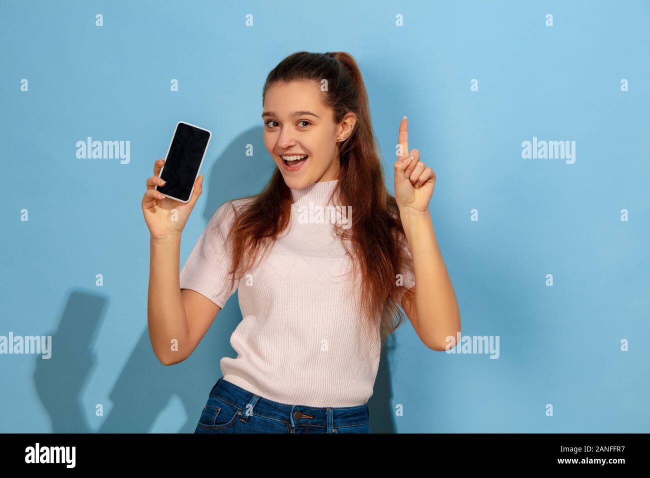 Showing phone screen, pointing up. Caucasian teen girl's portrait on ...