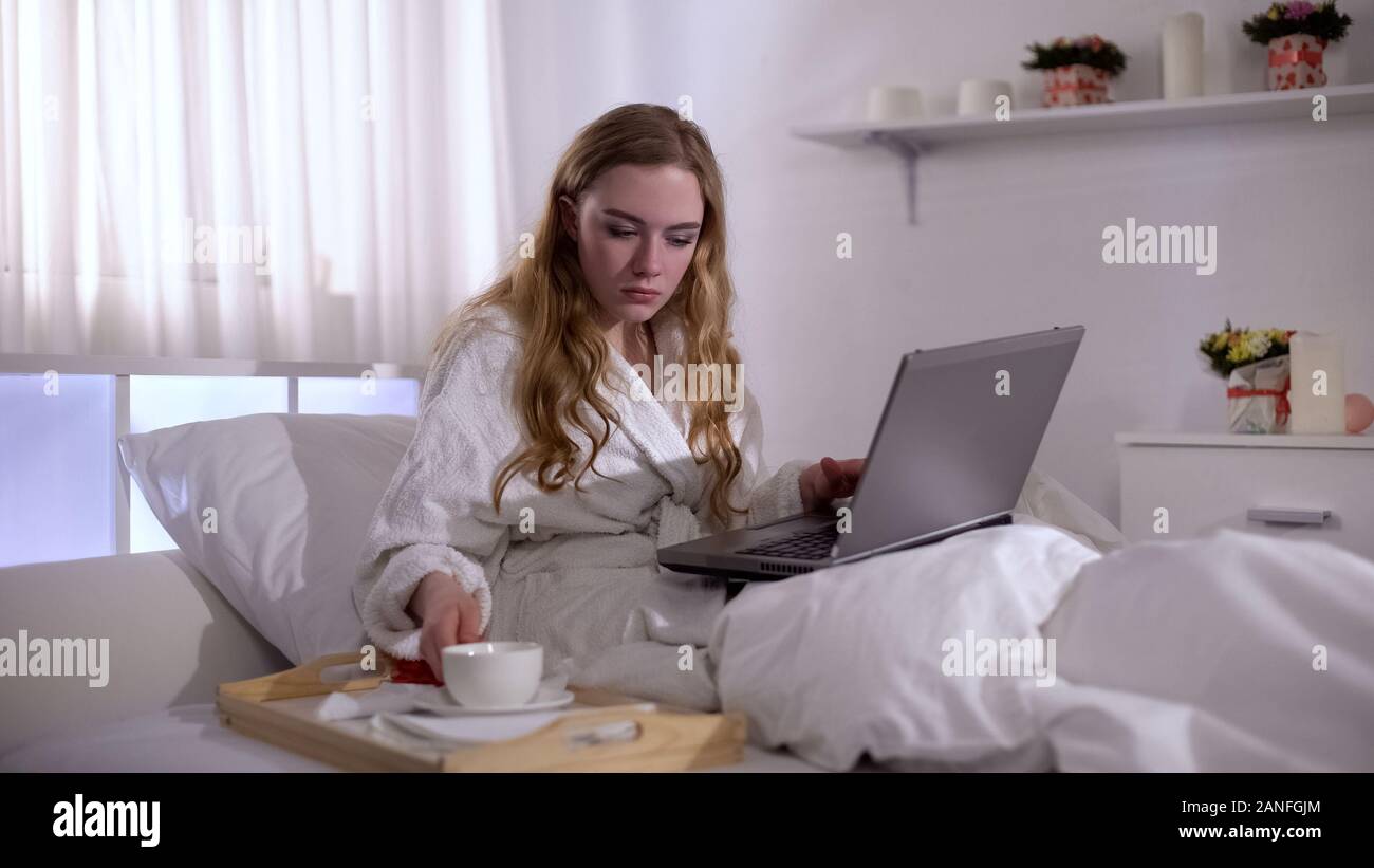 Girl in robe with coffee cup in bed working on laptop, freelance ...