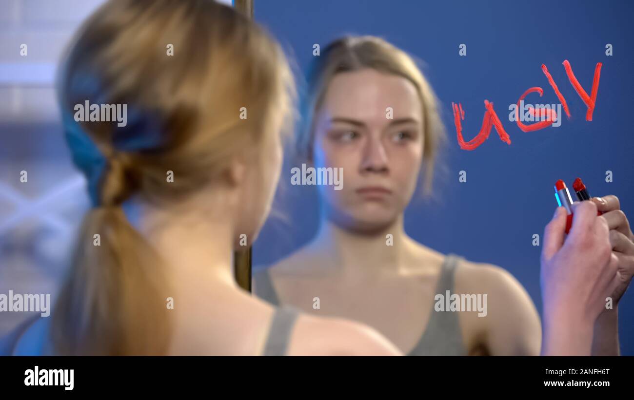 Upset college student writing word ugly by lipstick on mirror, bullying ...