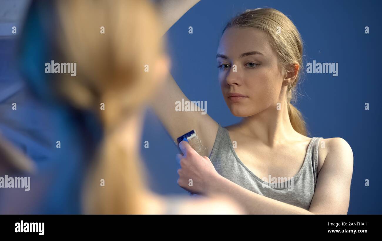 Pretty teenage female shaving armpit in front of mirror, personal ...