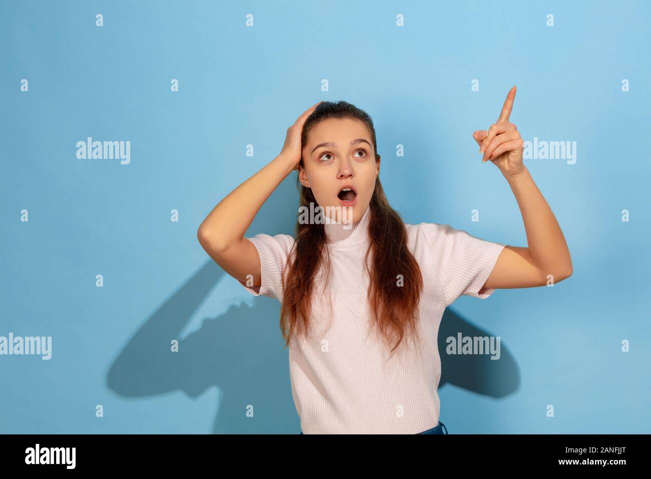 Shocked, scared, pointing up. Caucasian teen girl's portrait on blue ...
