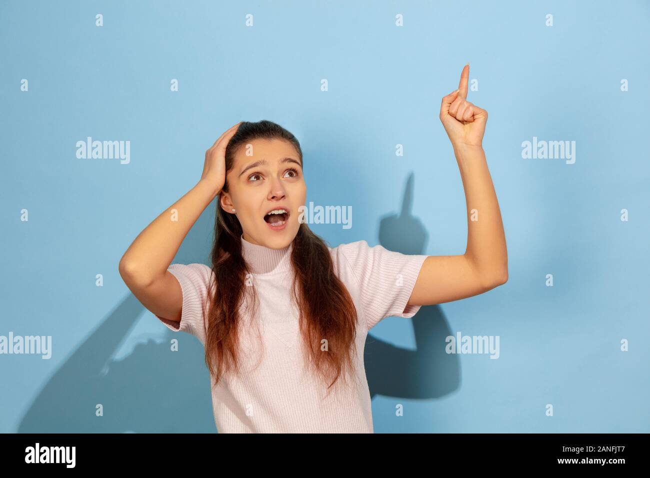 Shocked, scared, pointing up. Caucasian teen girl's portrait on blue ...
