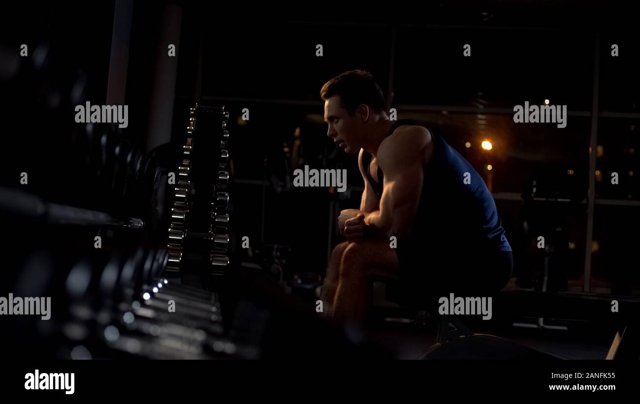 Strong bodybuilder resting after intensive workout with dumbbells at ...