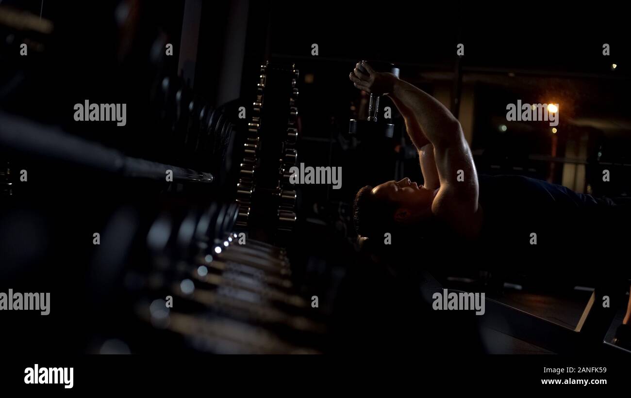 Purposeful athlete performing dumbbell pullovers, lying on bench, chest ...