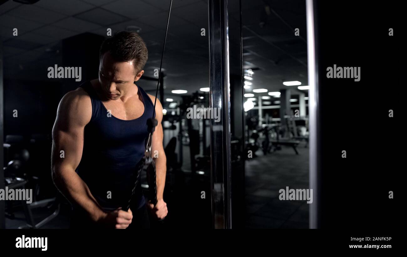 Athletic man training arm muscles, performing triceps cable pushdown ...