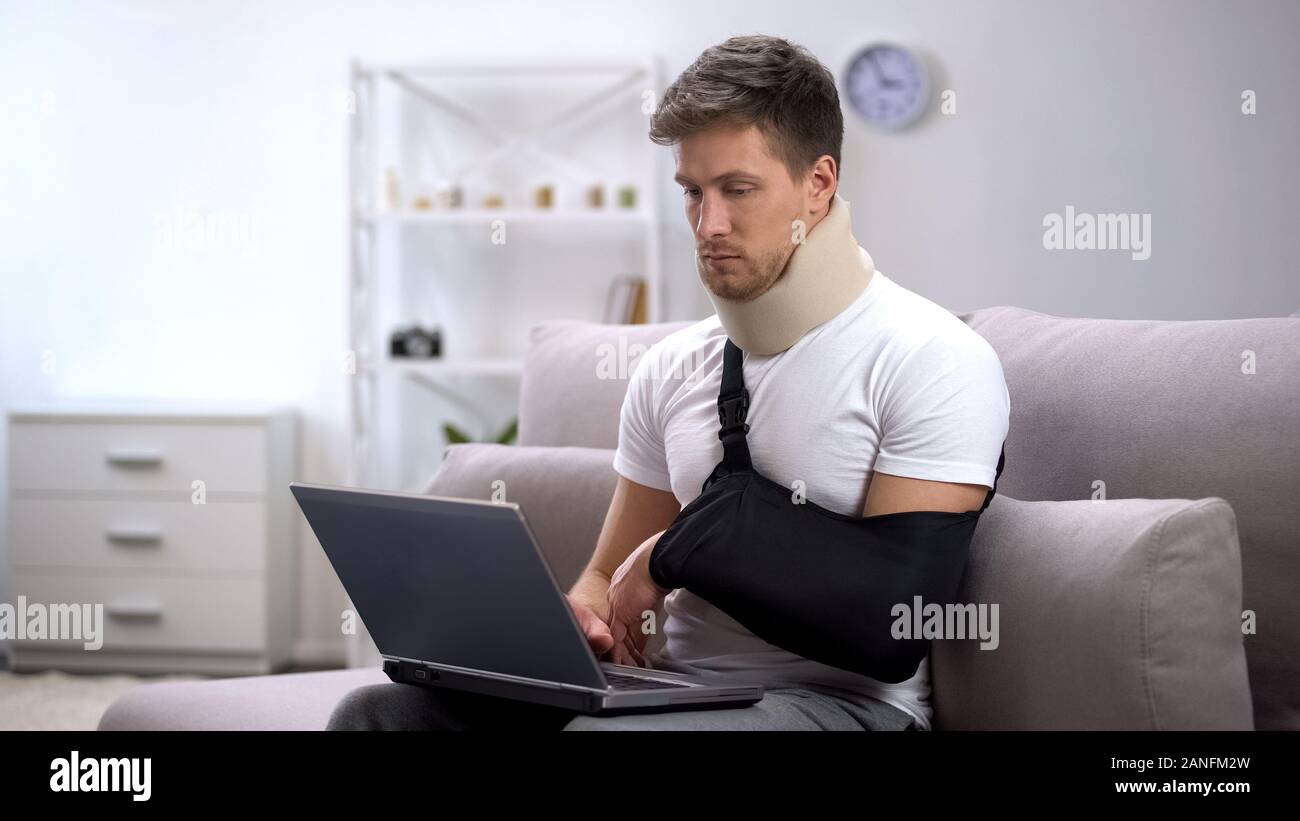 Male in foam cervical collar and arm sling typing one hand on laptop ...