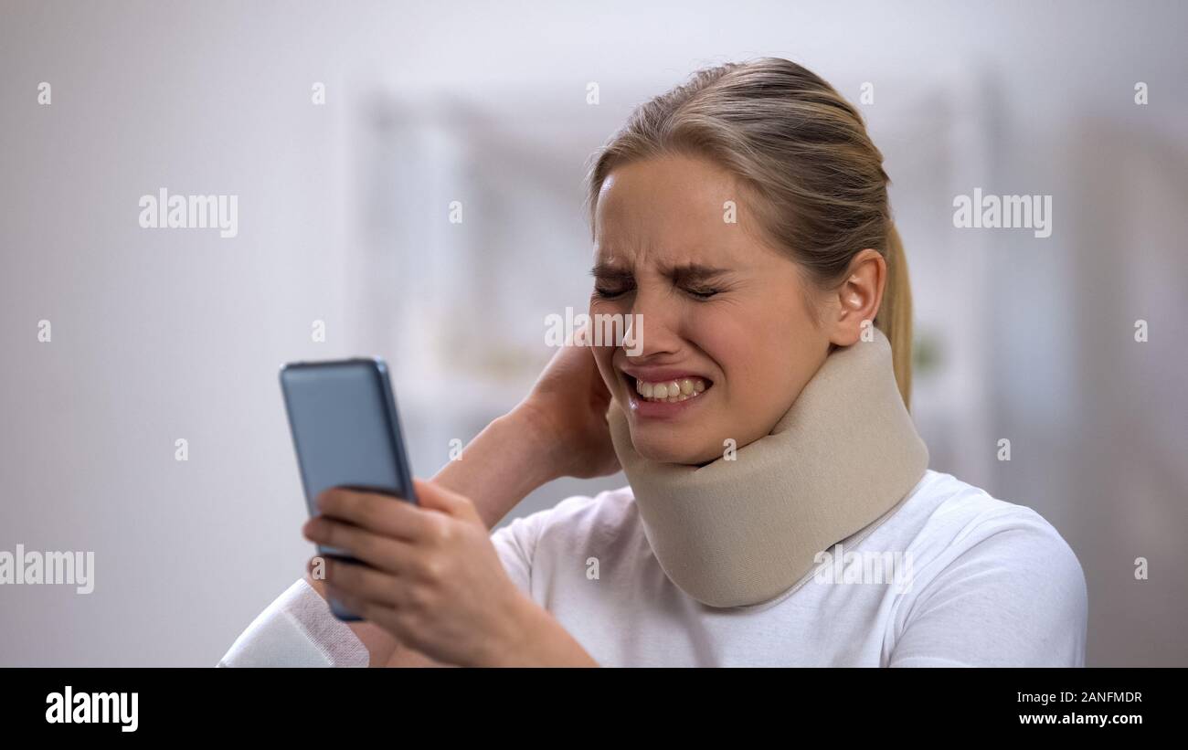 Woman in foam cervical collar reading message on phone feeling neck ...