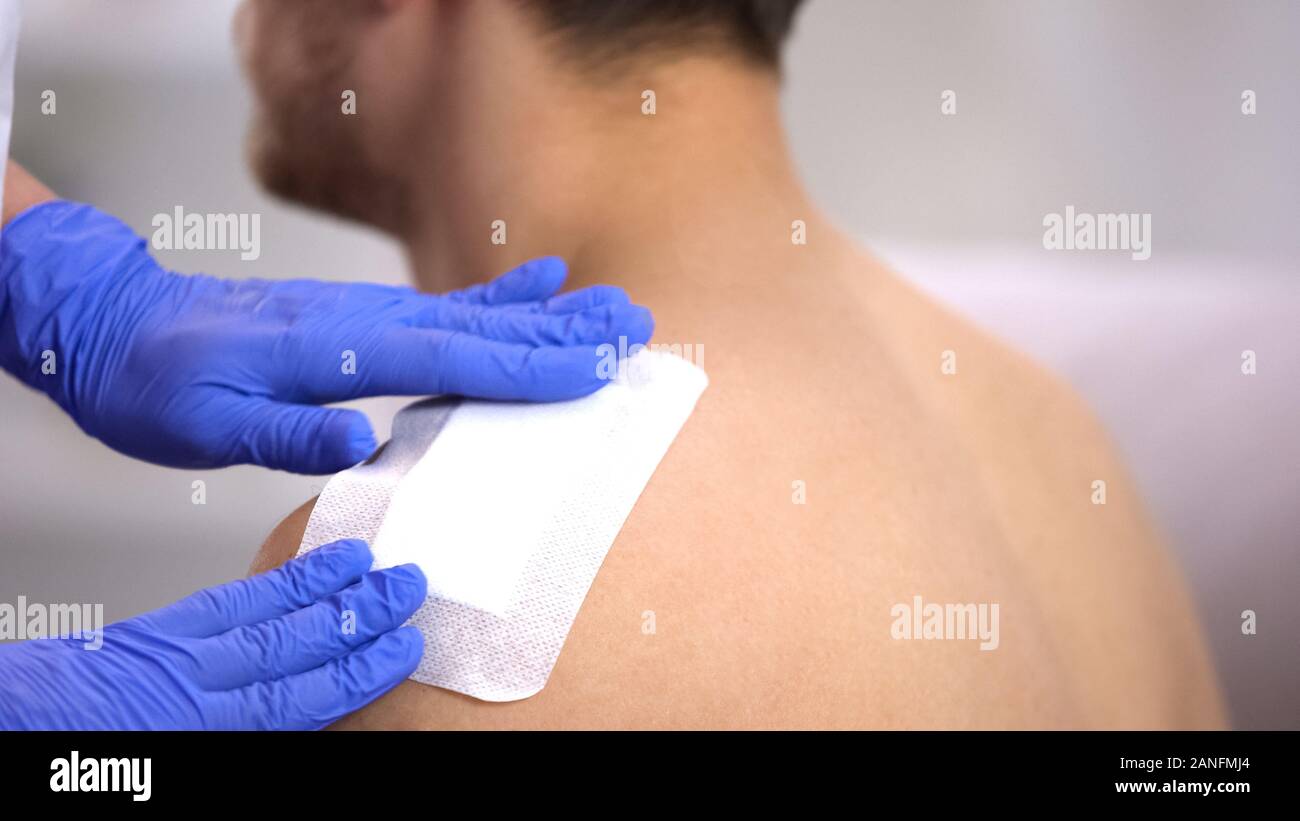 Doctor hands applying adhesive bandage on injured shoulder of male ...