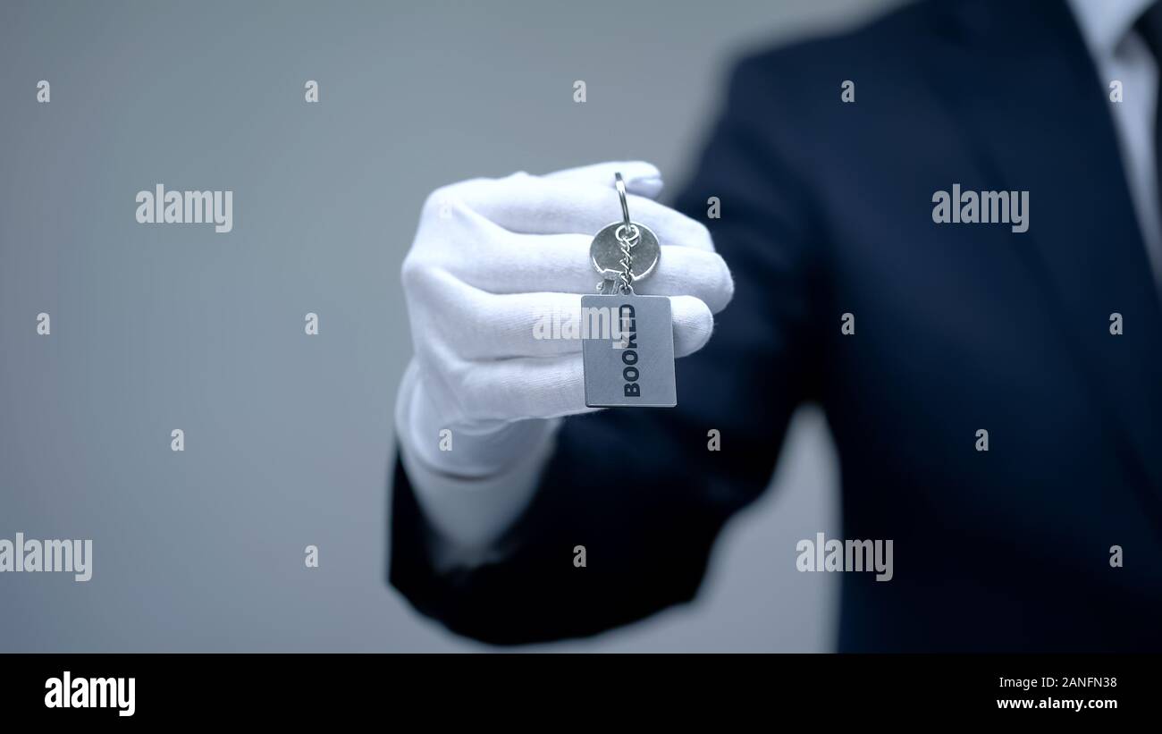 Booked word on keychain in receptionist hand, luxury hotel services ...