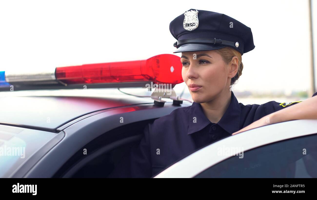 Strong lady in police uniform standing near patrol car, protecting law ...