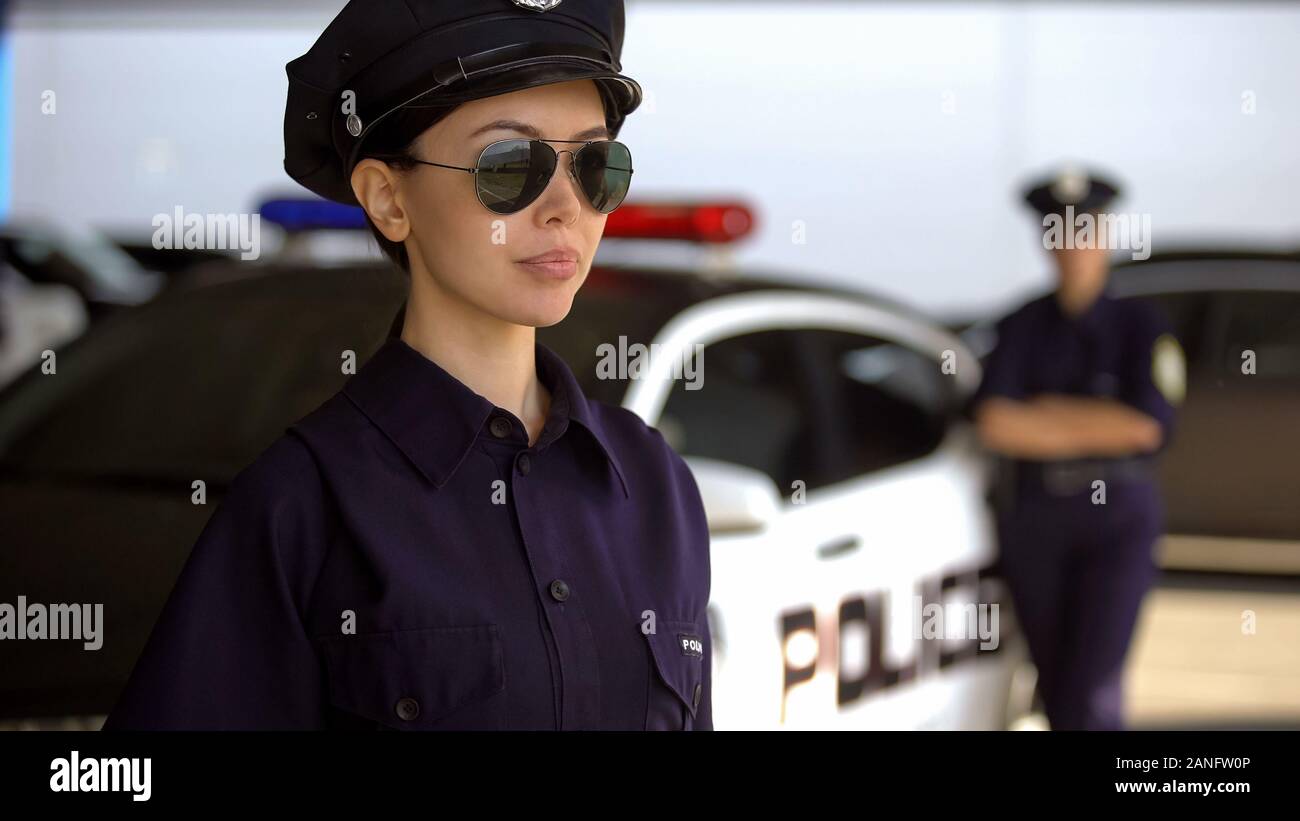 Serious police officer patrolling streets, partner near car on ...