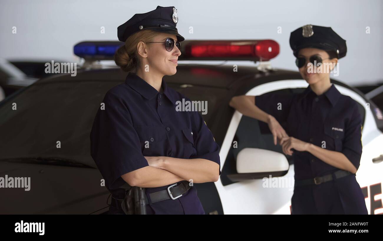 Positive police women standing near car, talking and smiling, break ...