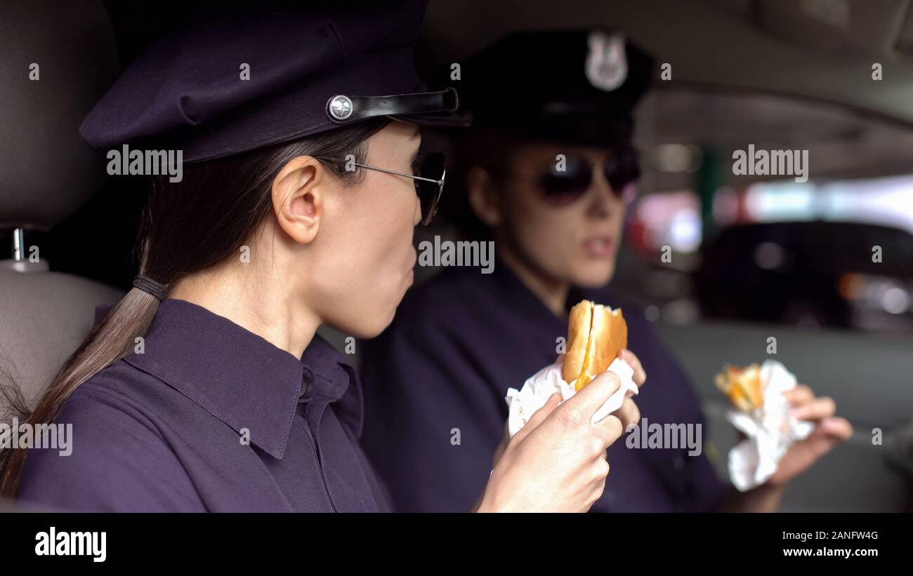 Policewomen on duty having lunch, eating burgers in patrol car ...