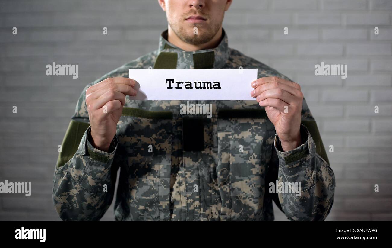 Trauma word written on sign in hands of male soldier, damage to body ...