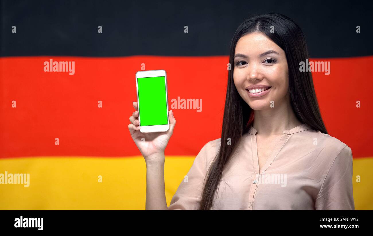Woman showing smartphone with green screen, German flag on background ...