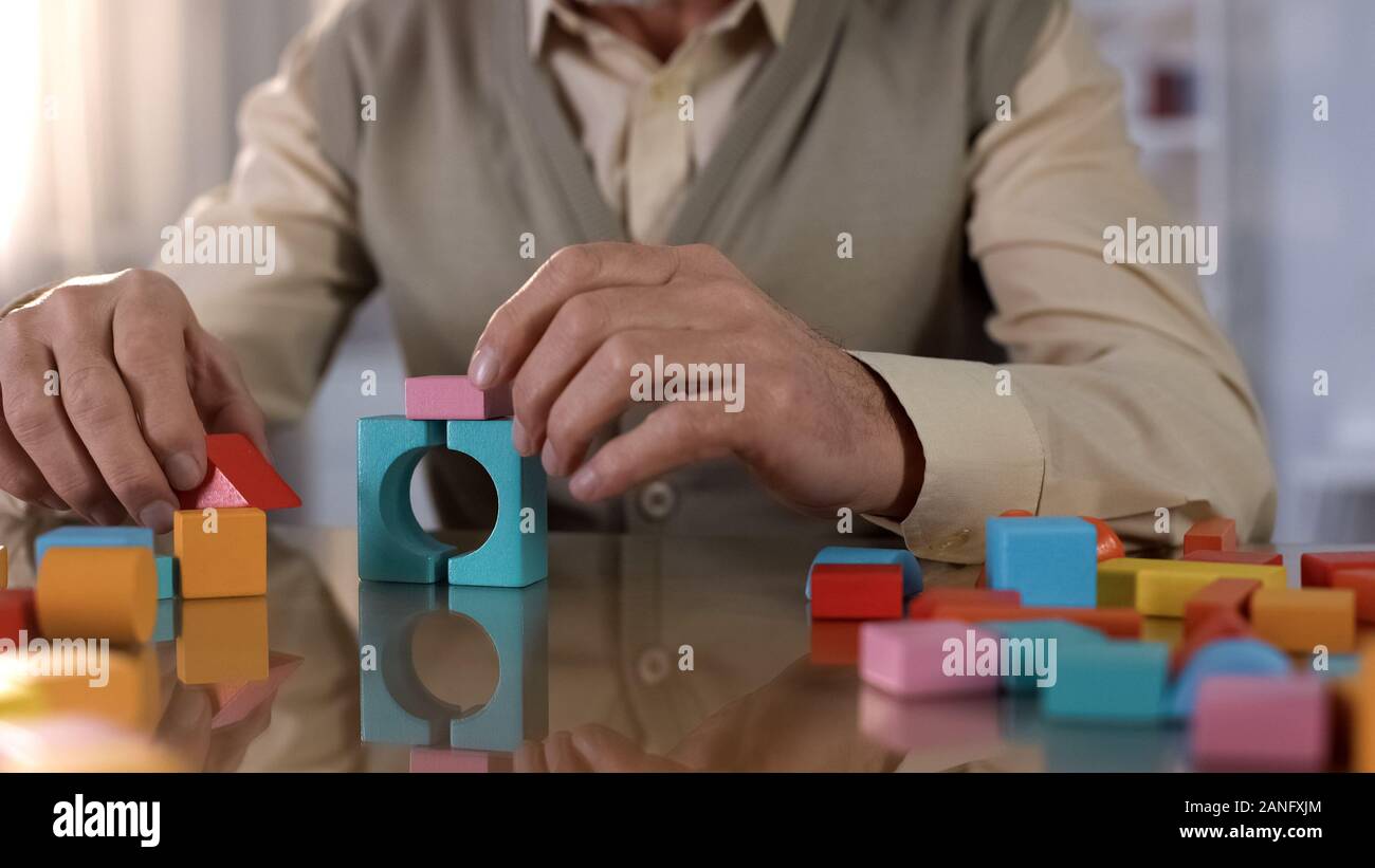Elderly male making house colored wooden cubes, concentration exercise ...