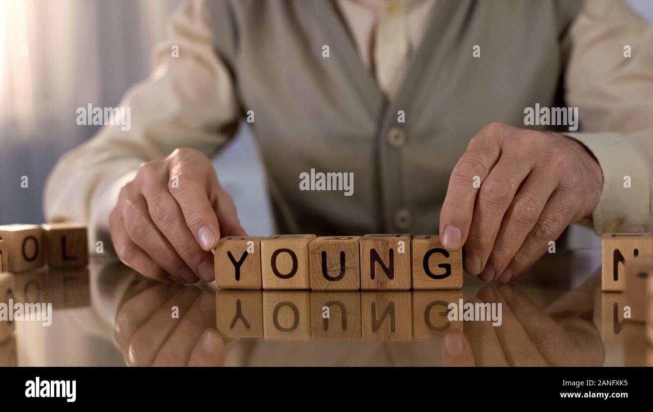 Grandfather making word young of wooden cubes on table, old age ...