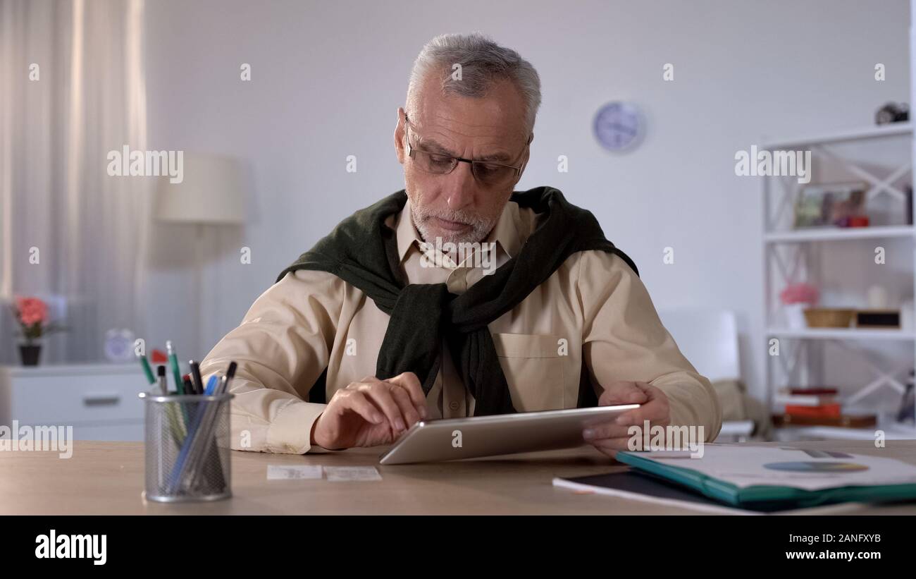 Old man entering data from checks into tablet, counting budget and ...