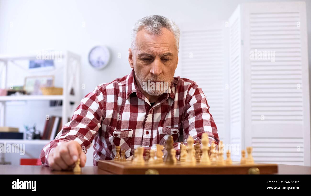 Concentrated old man playing chess alone, preparing for competition ...