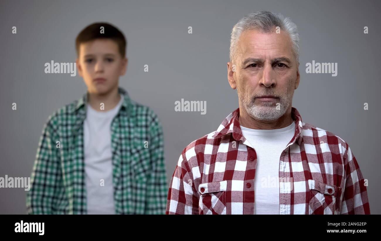 Aged male looking to camera, little boy standing behind, retirement age ...