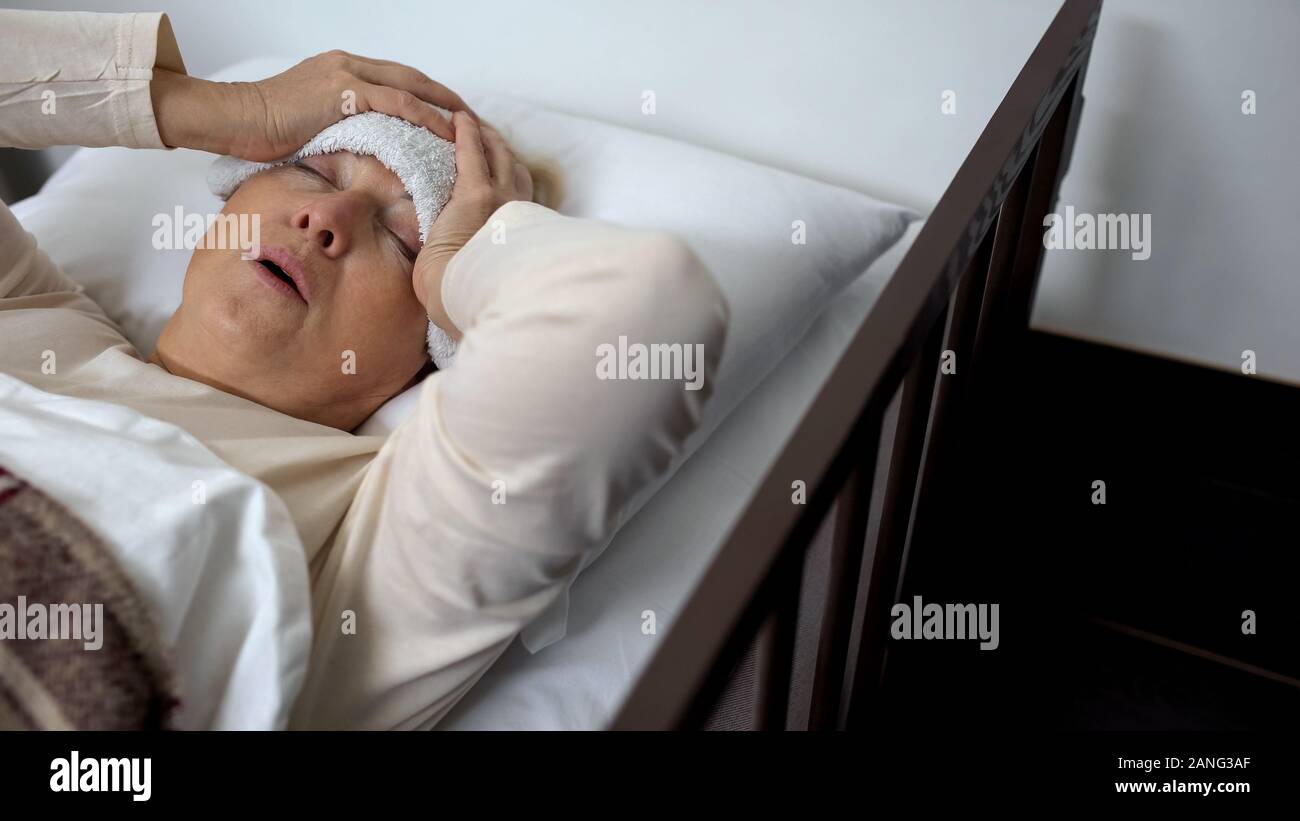 Elderly lady lying in bed with forehead compress and suffering terrible ...