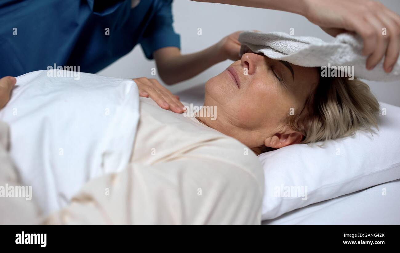 Sick woman suffering from fever and ravings, nurse putting compress on ...