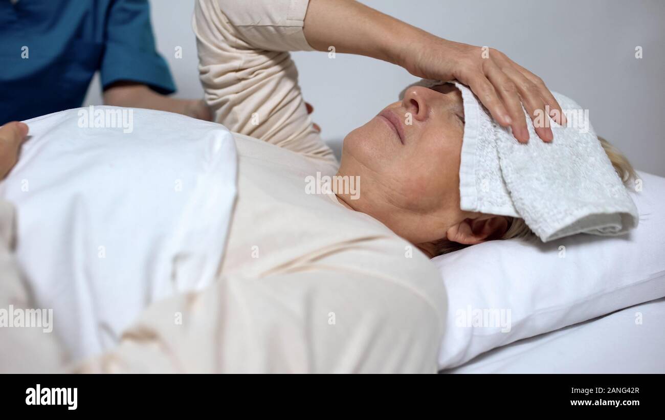 Female with compress on forehead suffering fever, nurse looking after ...