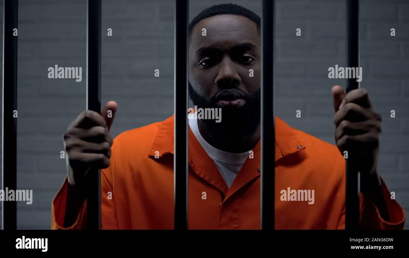 African-american male prisoner holding bars and looking to camera ...