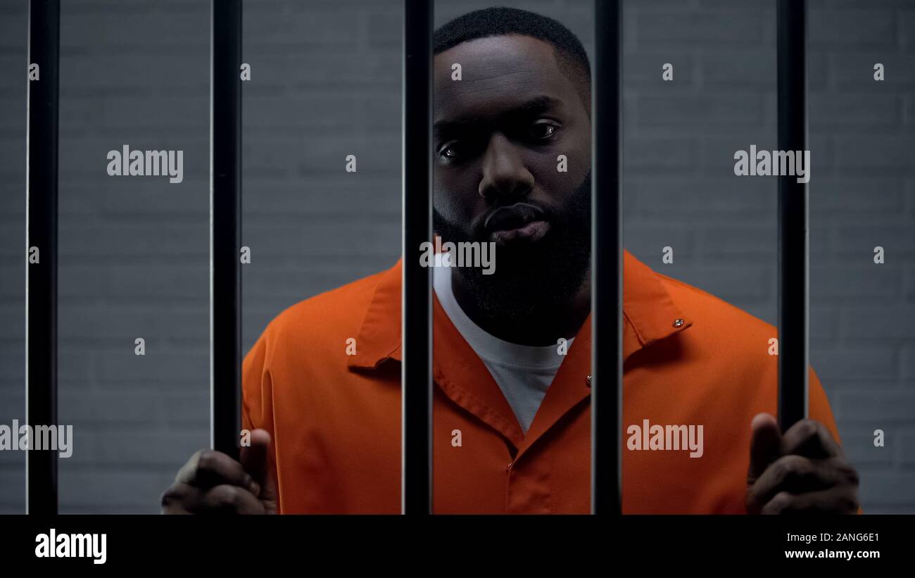 Black male prisoner waiting for sentence in prison cell, looking sadly ...