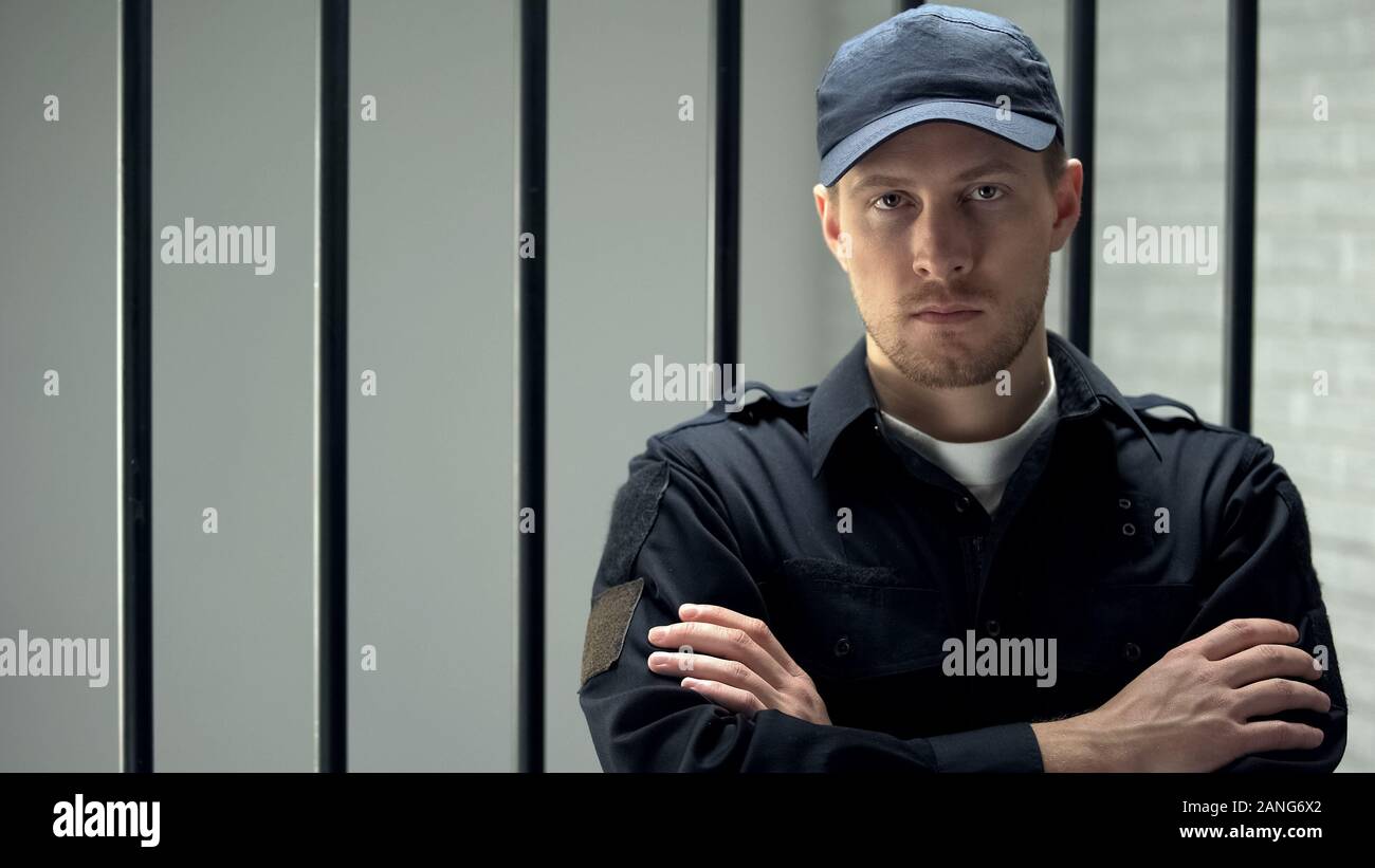 Brave jail guard looking at camera standing near cell, dangerous ...
