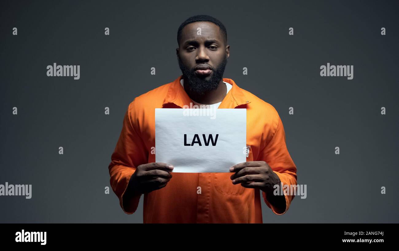 Black imprisoned man holding law sign in cell, looking to camera, human ...