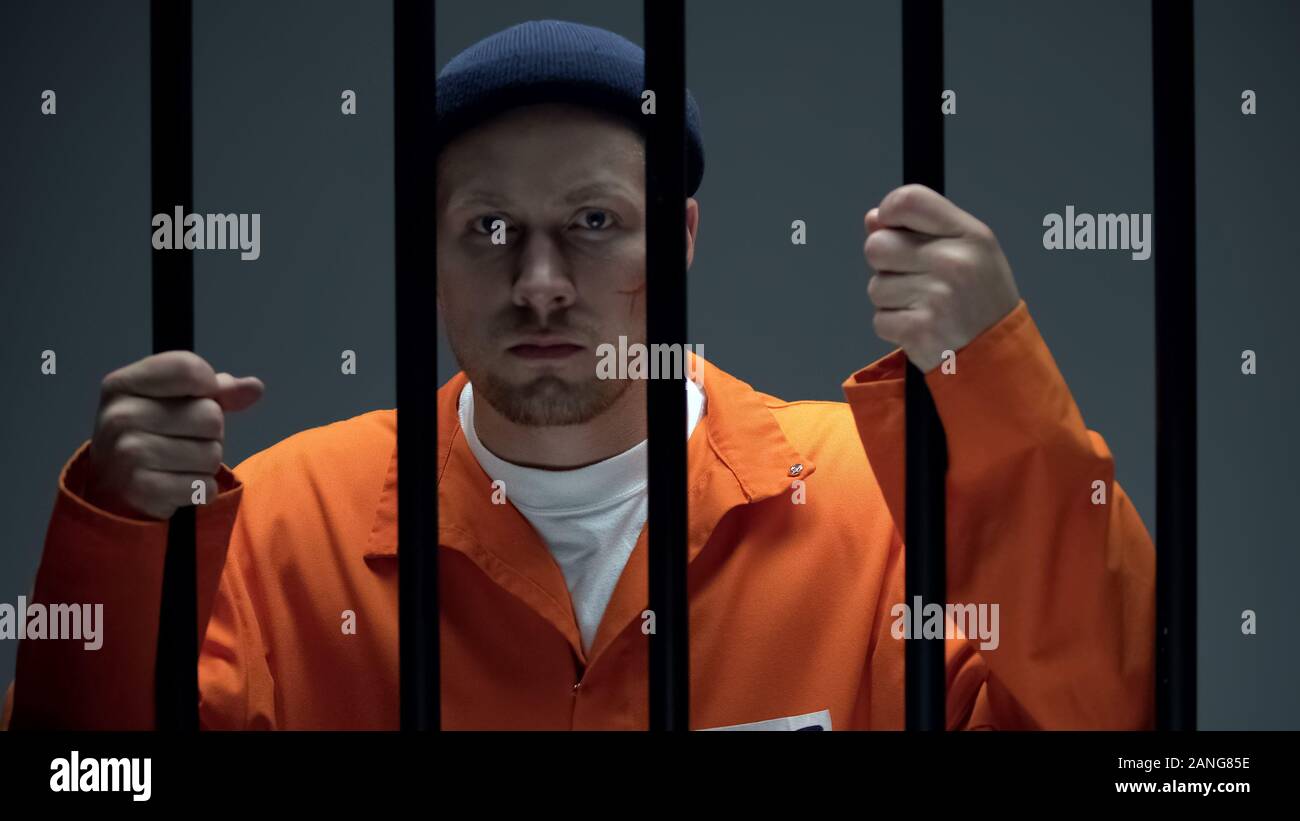 Dangerous imprisoned criminal with scar on face holding bars looking at ...