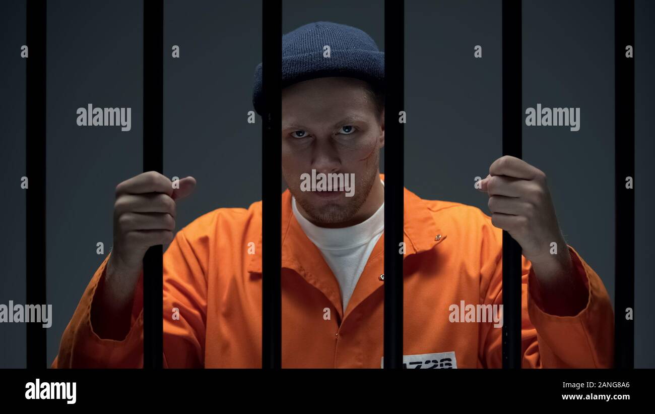 Angry Caucasian prisoner with scared face looking through cell bars ...
