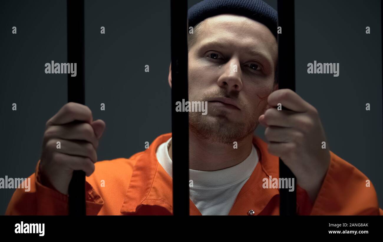 Crying prisoner holding bars and looking to camera, feeling guilty and ...