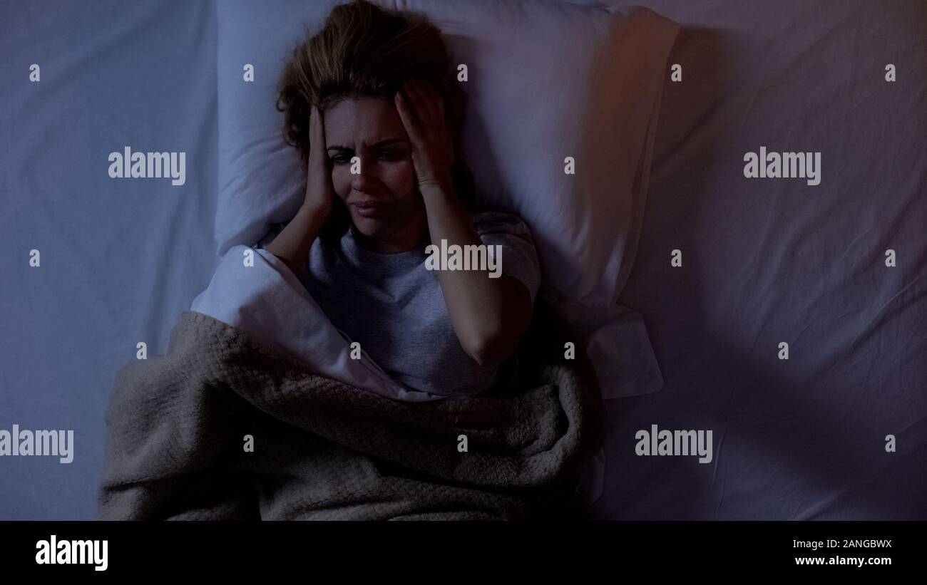 Woman having terrible headache lying in bed at night, strong migraine ...