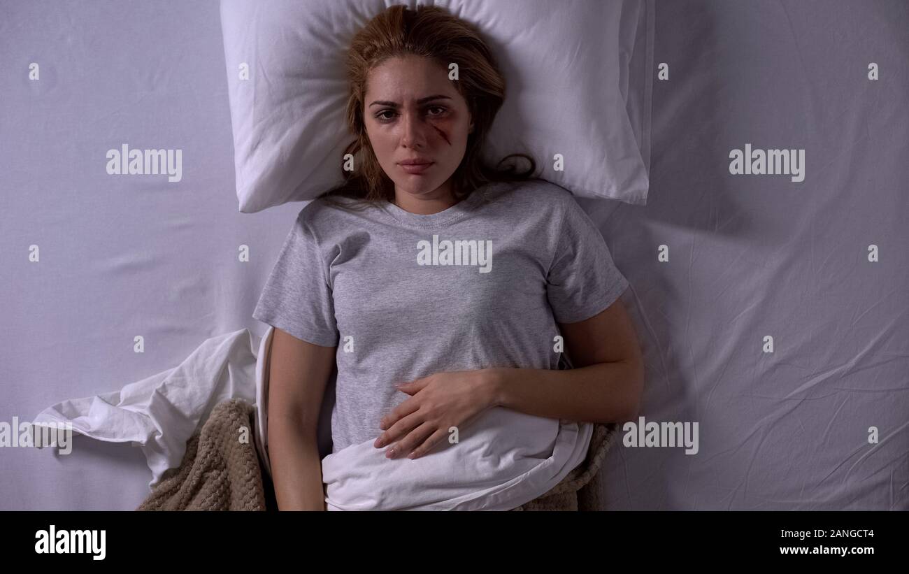 Desperate female victim looking in camera, lying in bed top view ...