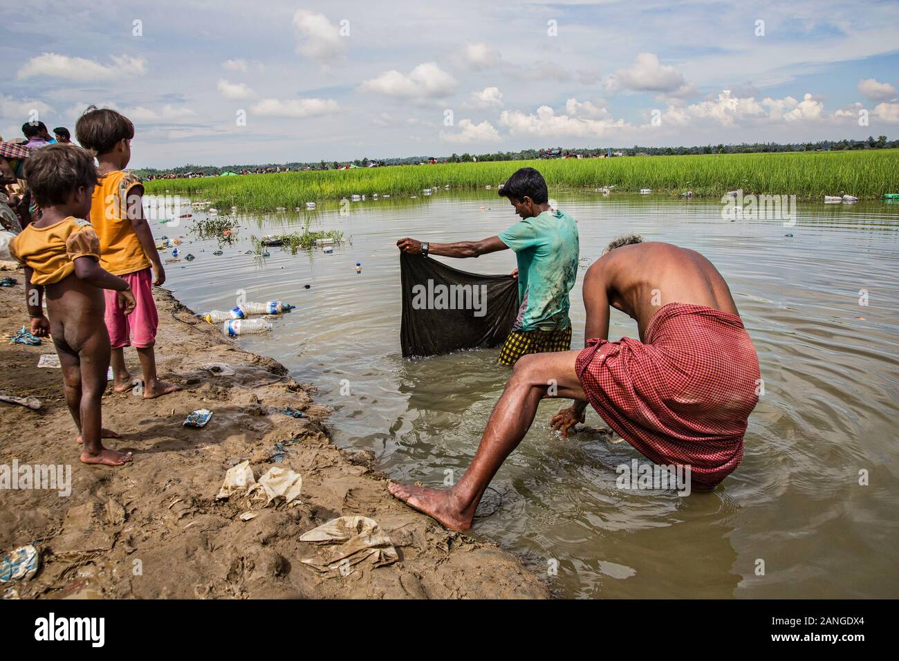 Rohingya refugee, in Bangladesh, washing their clothes in a rice field ...
