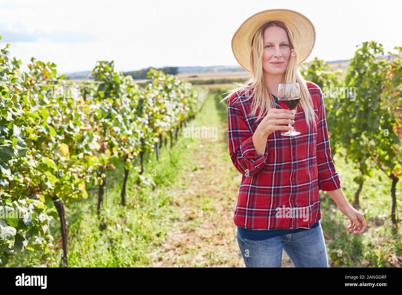 Young woman in the vineyard with a glass of red wine between vines ...