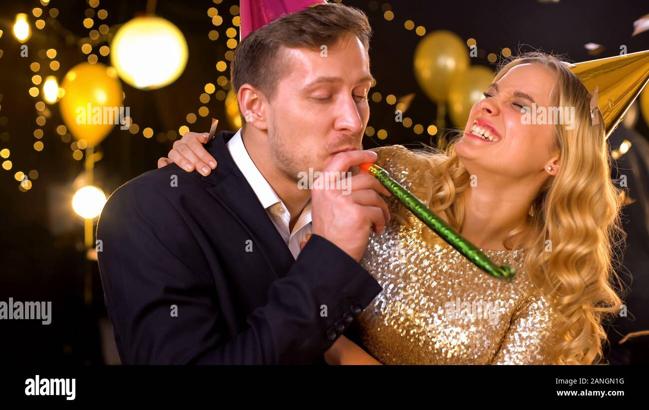 Carefree man and woman enjoying birthday party blowing party horn ...
