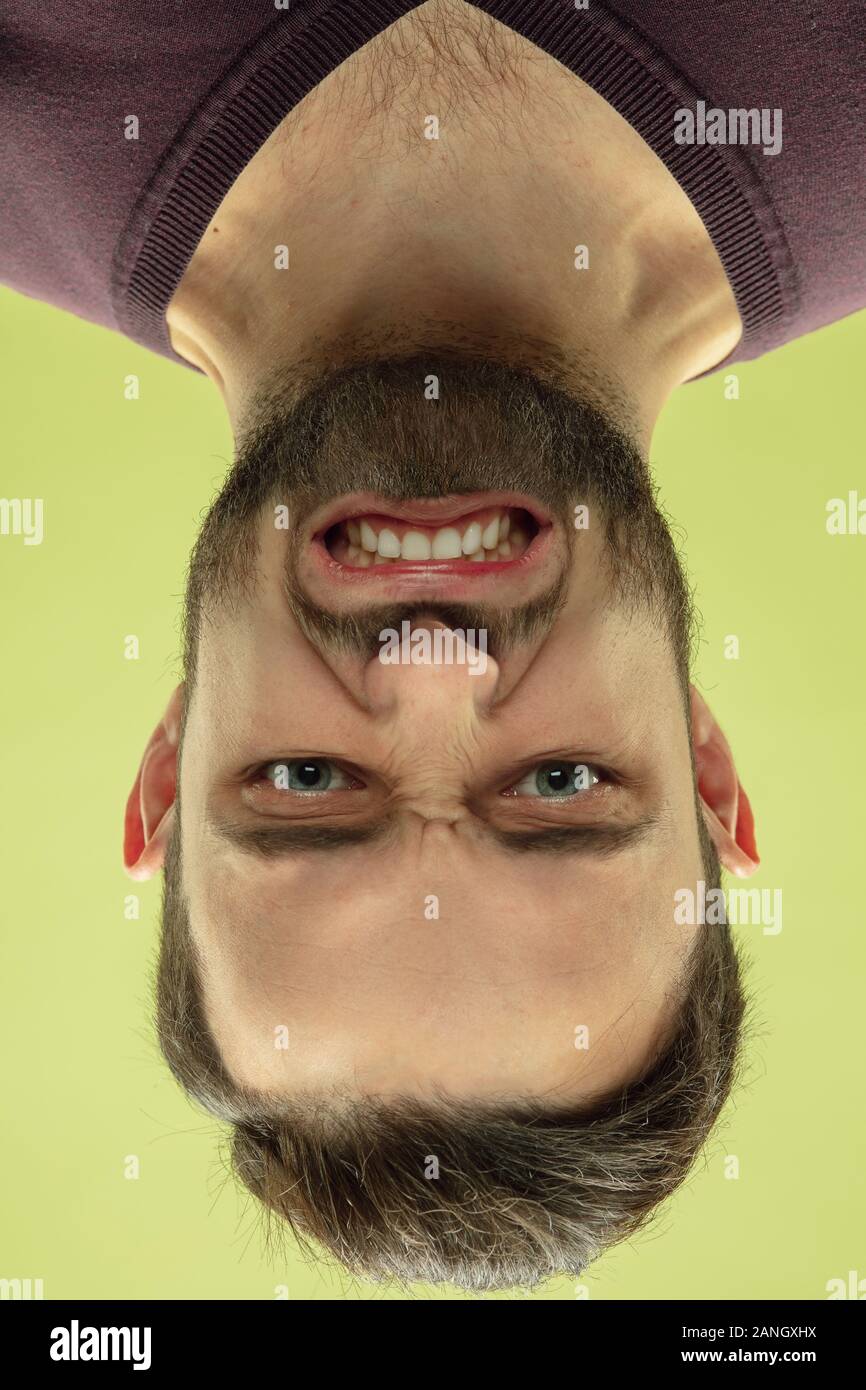 Looks angry, scary. Inverted portrait of caucasian young man on yellow ...