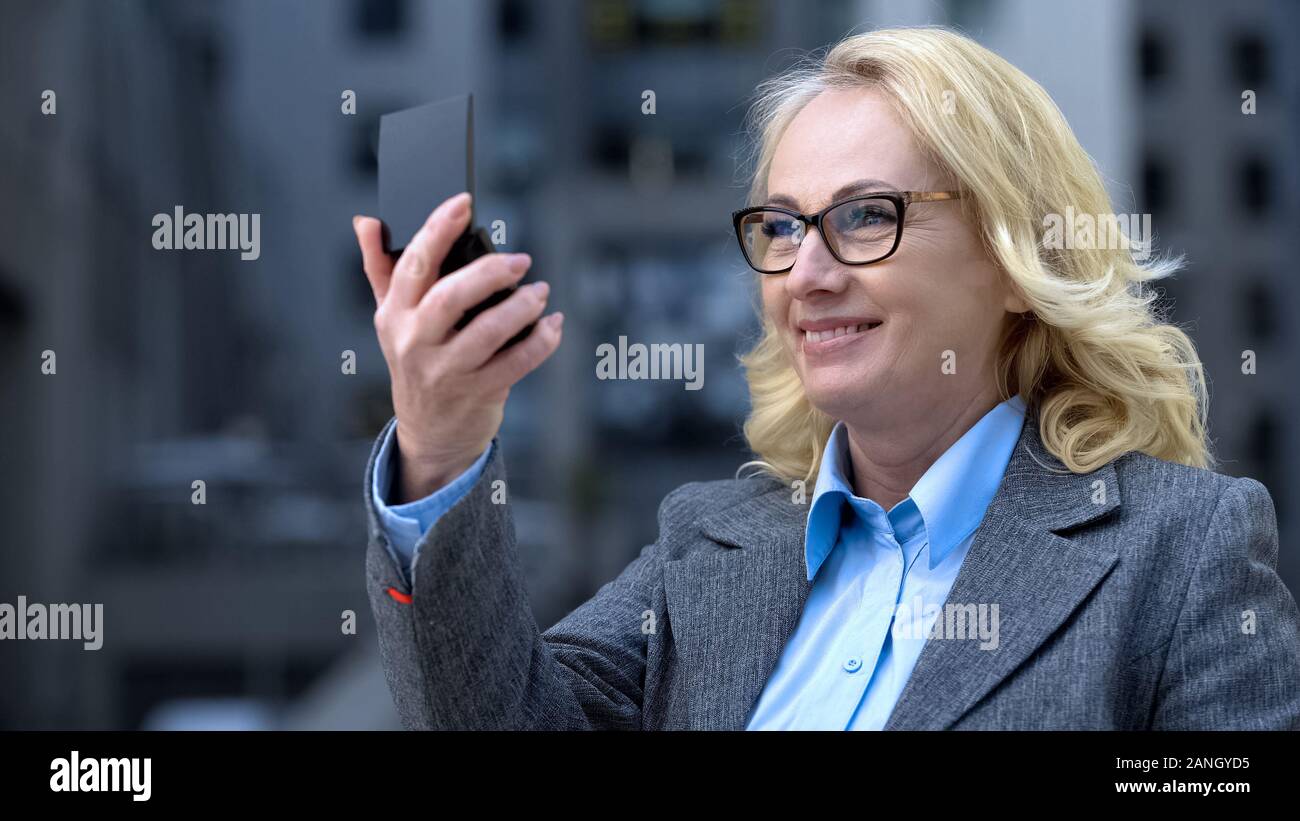 Happy beautiful lady in suit looking in small mirror, satisfied with ...