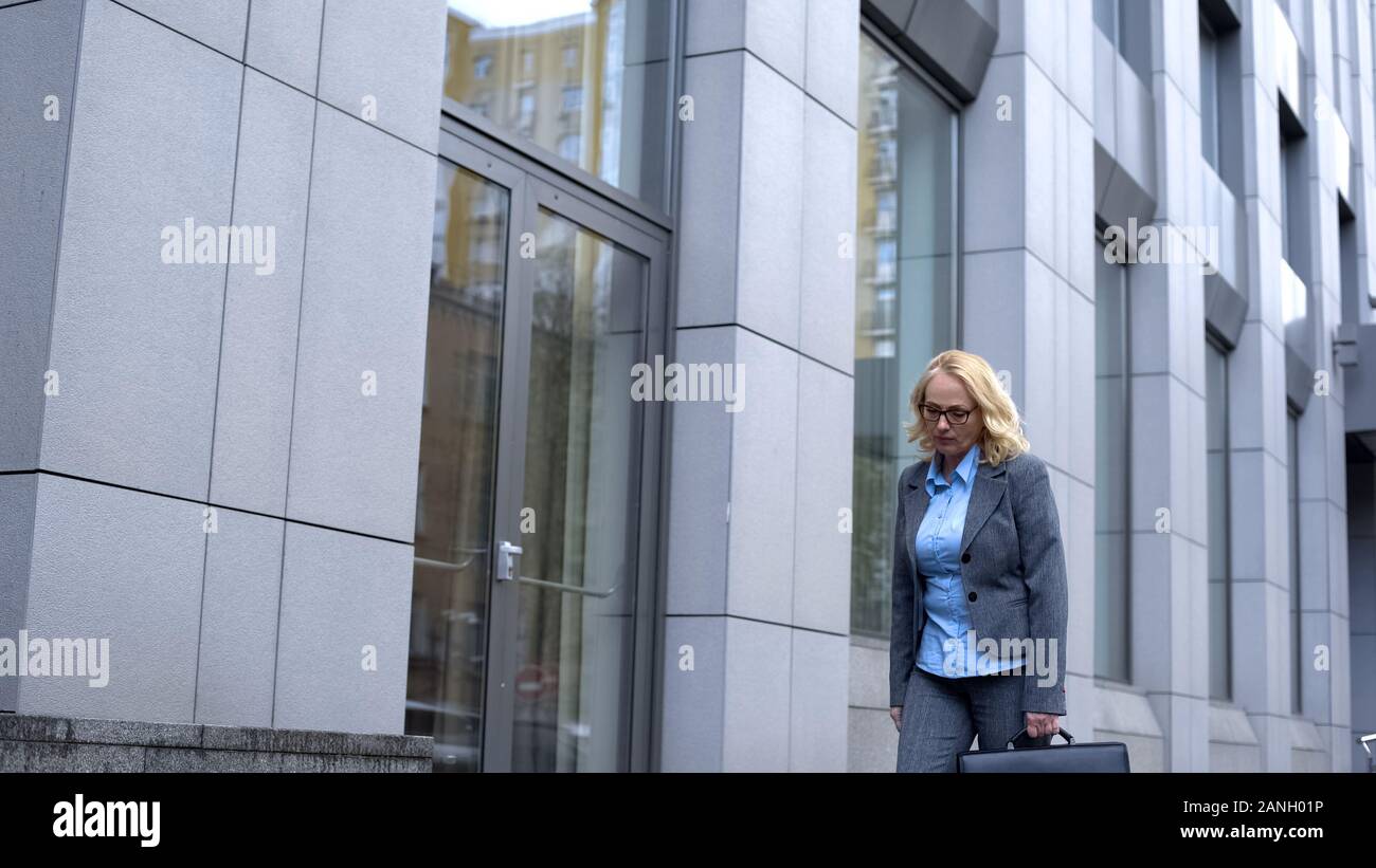 Sad aged woman getting work walking along office building, occupational ...